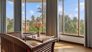 Um quarto com uma mesa e cadeiras de madeira, um vaso com flores e janelas amplas com cortinas.