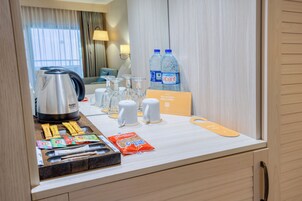 Minibar de um quarto de hotel, com chaleira, copos, garrafas de água, uma bandeja com lanches e um cartão de boas-vindas.