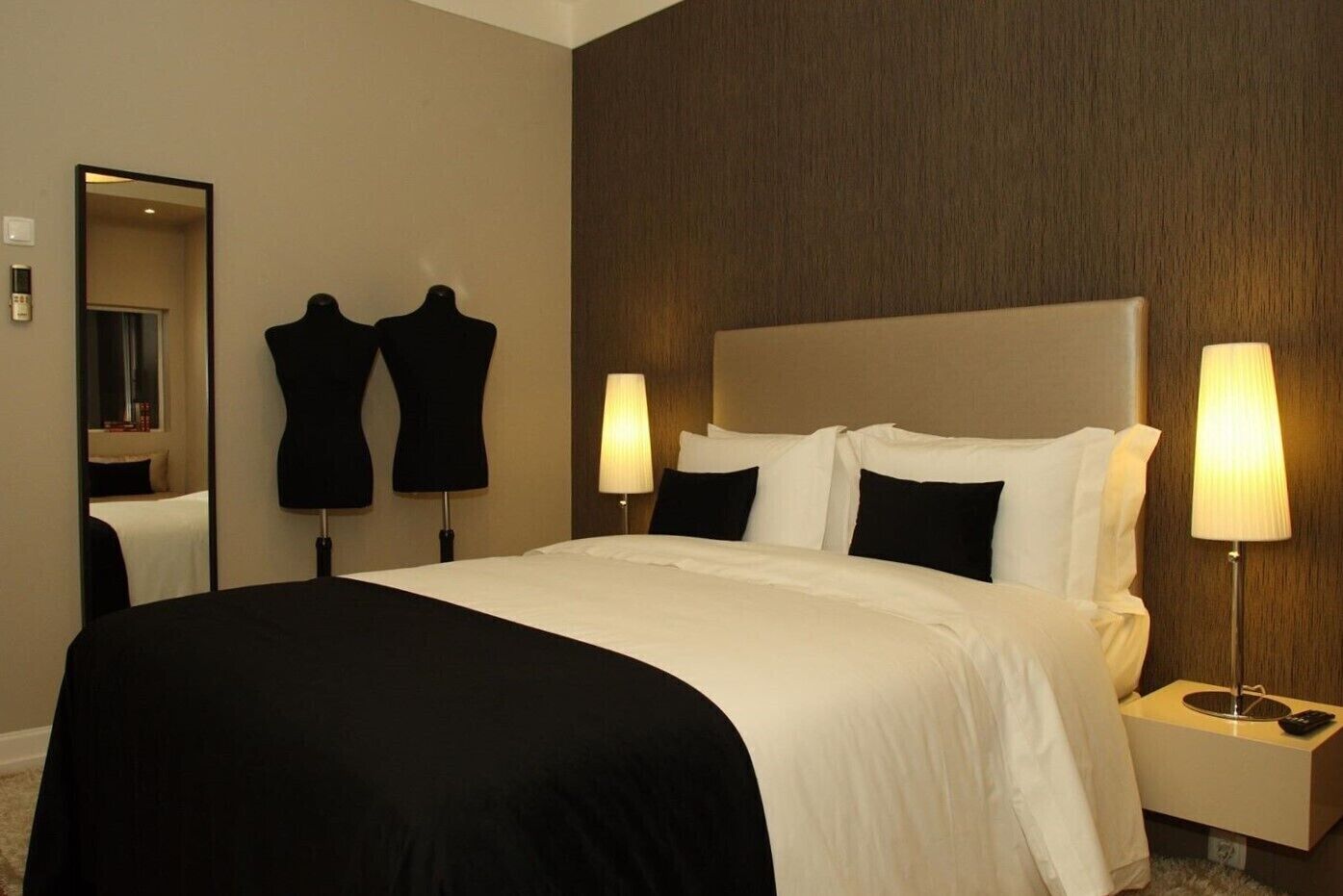 Quarto de hotel com uma cama grande, duas luminárias de cabeceira, um espelho e uma parede de destaque em madeira.