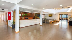 Uma área de recepção de hotel com design moderno, balcão de atendimento, espaço para sentar e vista para o mar.