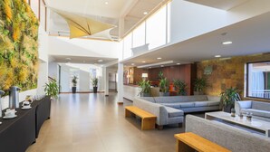 Um hall espaçoso com teto alto, balcão de recepção, áreas de estar e uma grande parede verde com plantas.
