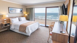 Quarto de hotel com cama, escrivaninha e vista para o oceano.
