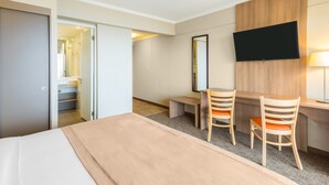 Quarto de hotel com uma cama, uma mesa com duas cadeiras, uma televisão e um espelho.
