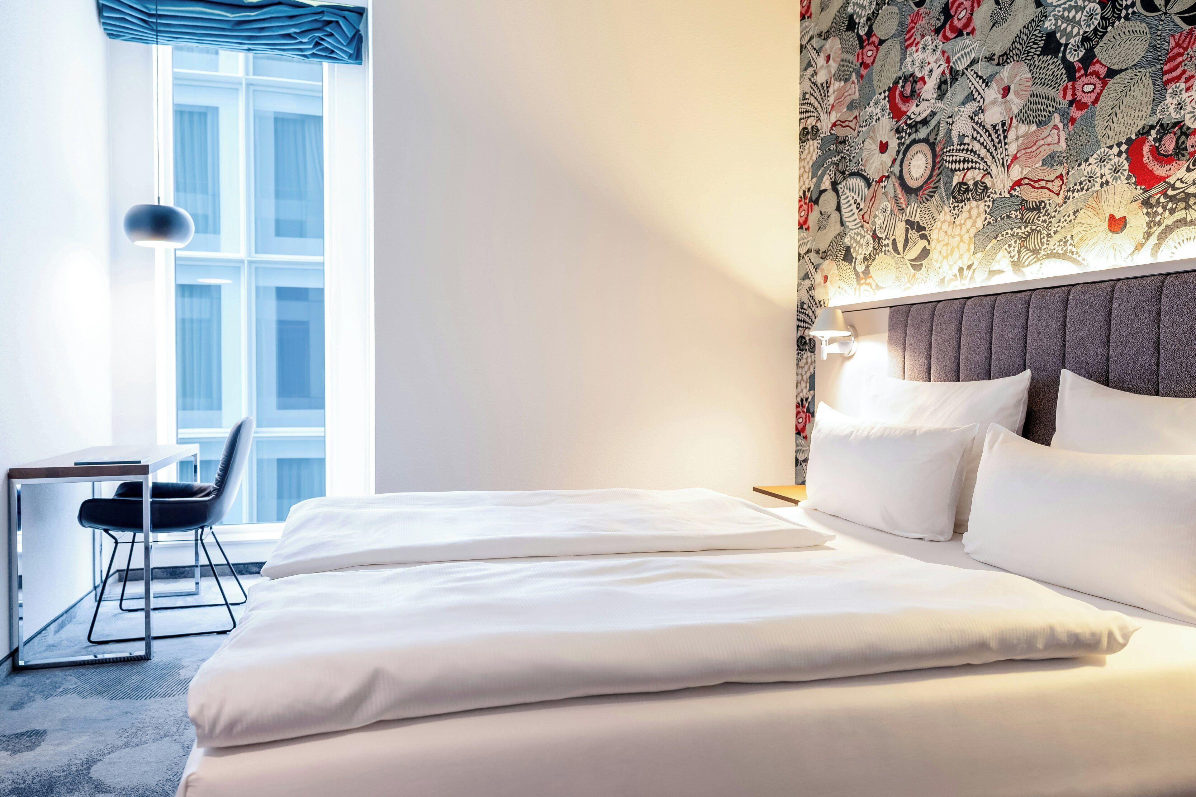 Quarto de hotel com uma cama, uma escrivaninha e uma cadeira.
