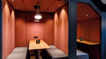 Uma área de estar pequena e fechada, com uma mesa e bancos, com iluminação embutida e uma luminária fixada na parede.