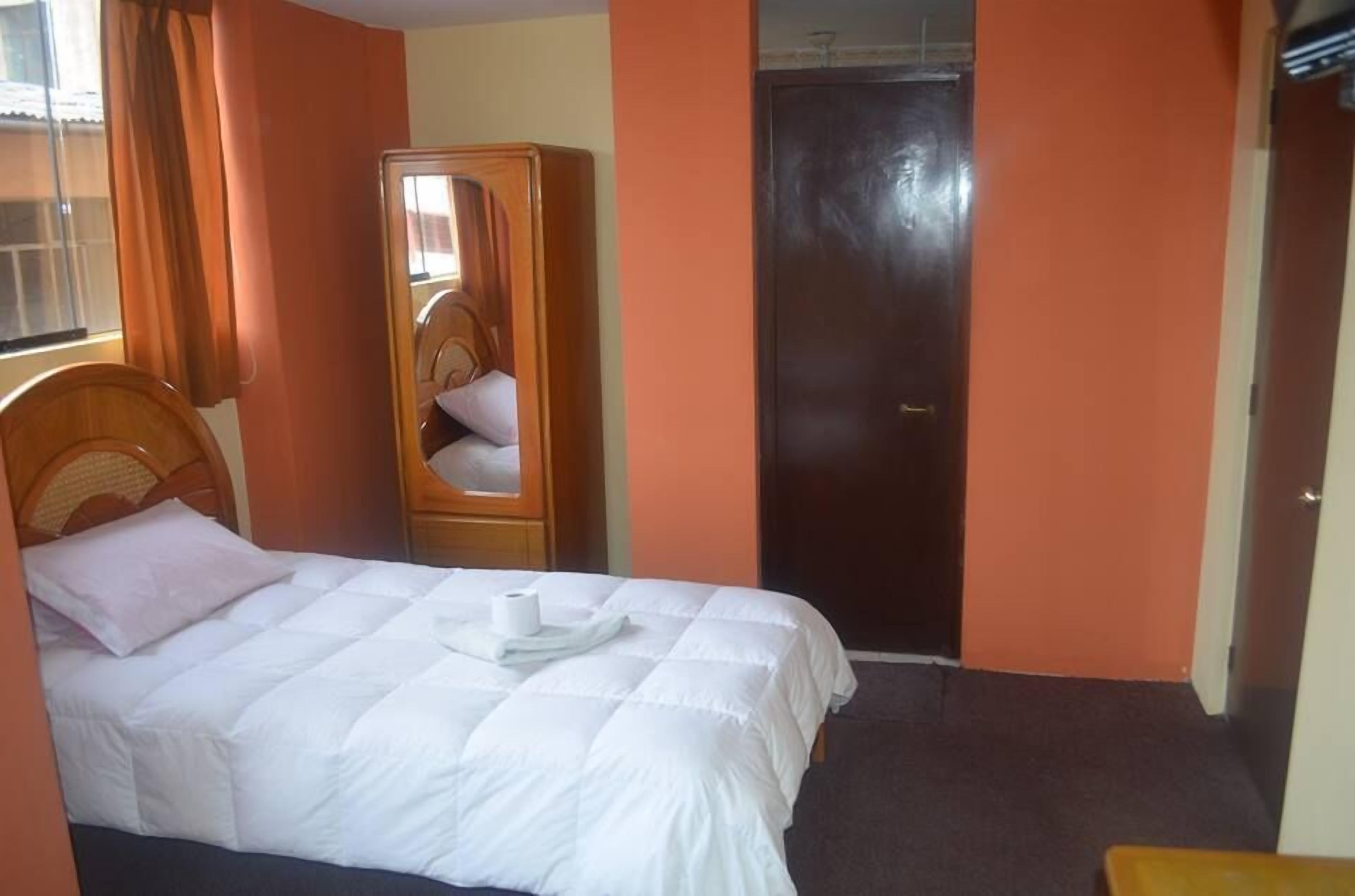 Quarto de hotel com cama, guarda-roupa de madeira, porta e janela com cortinas.