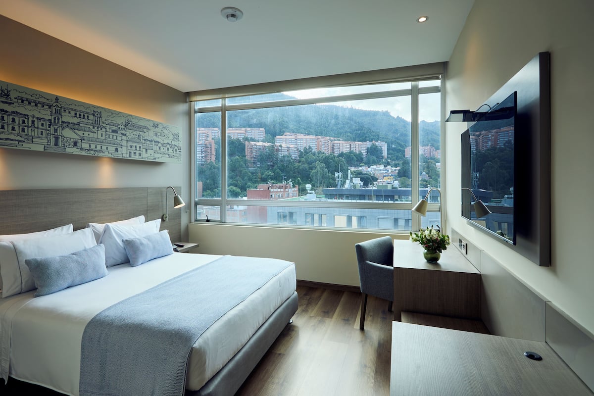 Quarto de hotel moderno com uma cama grande, uma escrivaninha e uma televisão.