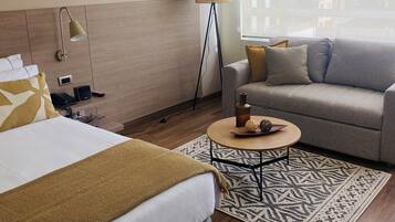 Quarto de hotel com cama, sofá, mesa de centro, luminária, quadro e vista da cidade.