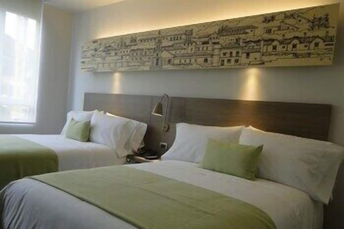 Quarto de hotel com duas camas, cabeceira, obra de arte pendurada na parede e uma janela.