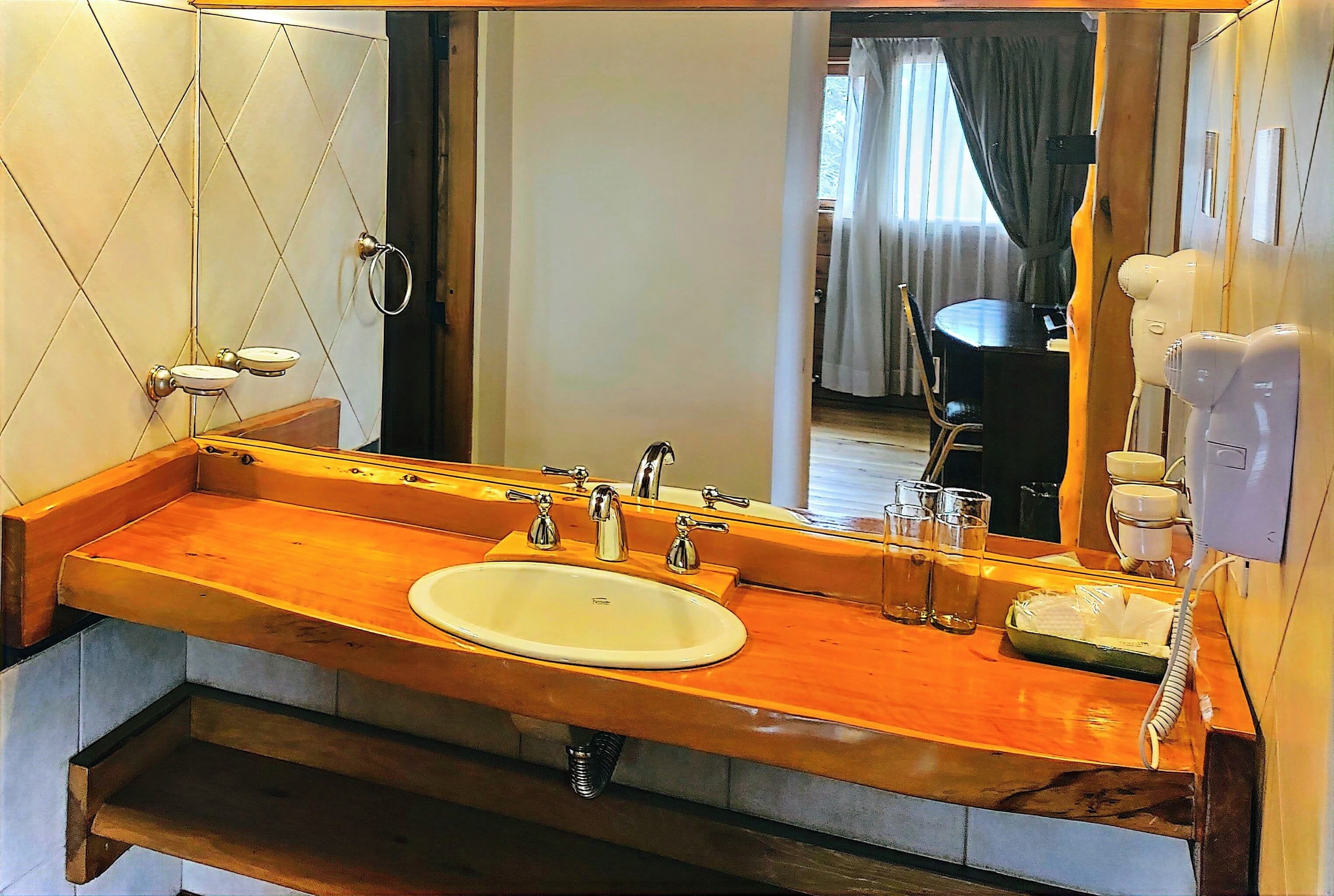 Casa de banho com toucador de madeira, pia branca, espelho e secador de cabelo na parede.