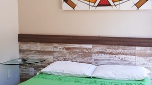 Cama bem arrumada com colcha verde e toalhas brancas, uma obra de arte na parede acima e cabeceira de madeira.