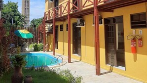 Um edifício amarelo com piscina, área de estar ao ar livre e estrutura metálica vermelha.
