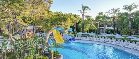 Uma piscina com escorregador, rodeada por palmeiras e espreguiçadeiras.
