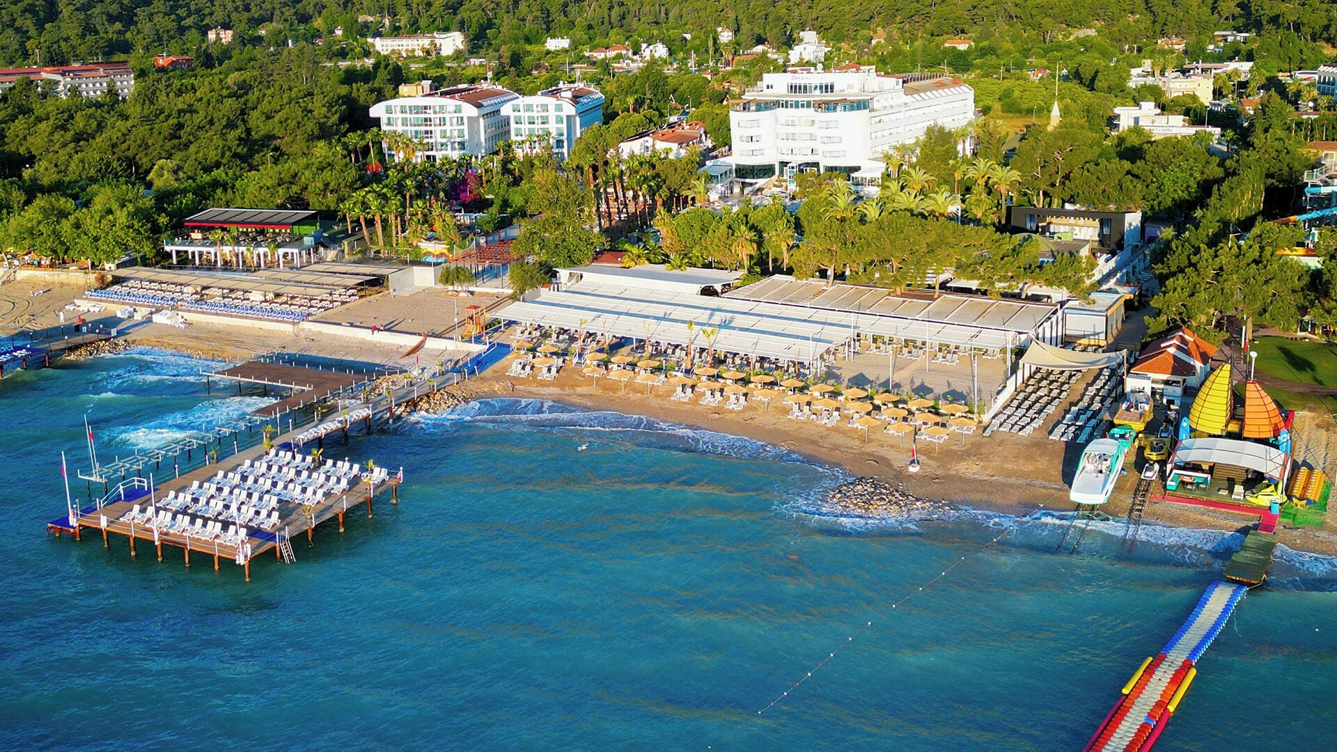 Vista aérea de um resort à beira-mar, com um cais, praia e vários edifícios.