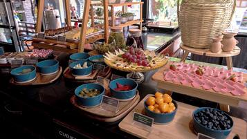 Buffet com diversas opções de comida, incluindo frutas, queijos e carnes.