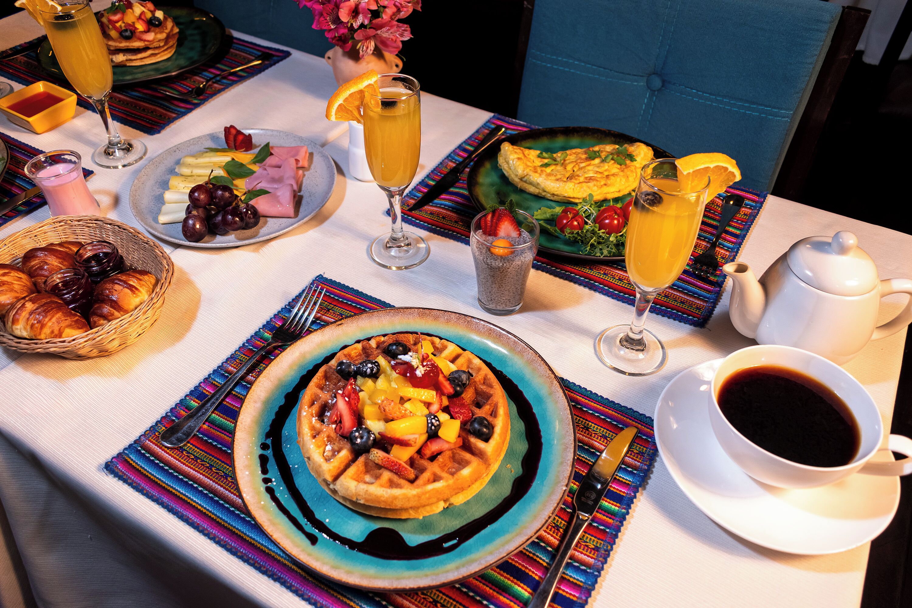Uma mesa de café da manhã com waffles, frutas e bebidas.