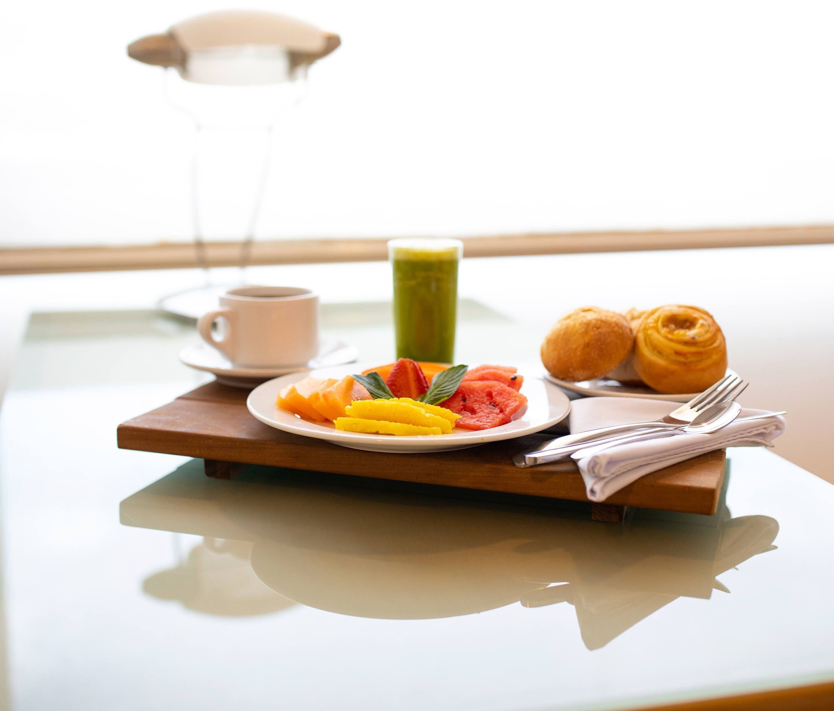 Uma bandeja de café da manhã com frutas, um smoothie verde, croissants e uma xícara de café sobre uma mesa.