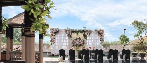Uma área à beira da piscina com um gazebo, um espaço de estar coberto e um painel de flores.