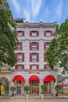 Fachada de hotel com design simétrico, várias janelas com persianas e uma entrada destacada com toldo.
