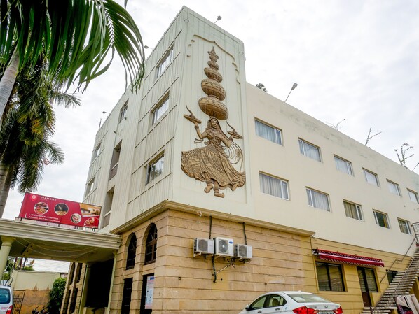 Um edifício de vários andares com um grande mural na fachada retratando uma figura tradicional, aparelhos de ar condicionado e uma escadaria visível.