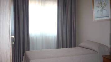 Quarto de hotel com cama, porta de madeira e janela com cortinas.