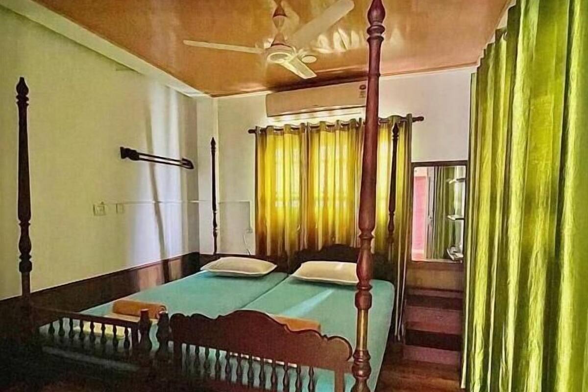 Uma cama de dossel com estrutura de madeira, um ventilador de teto e uma janela com cortinas amarelas.
