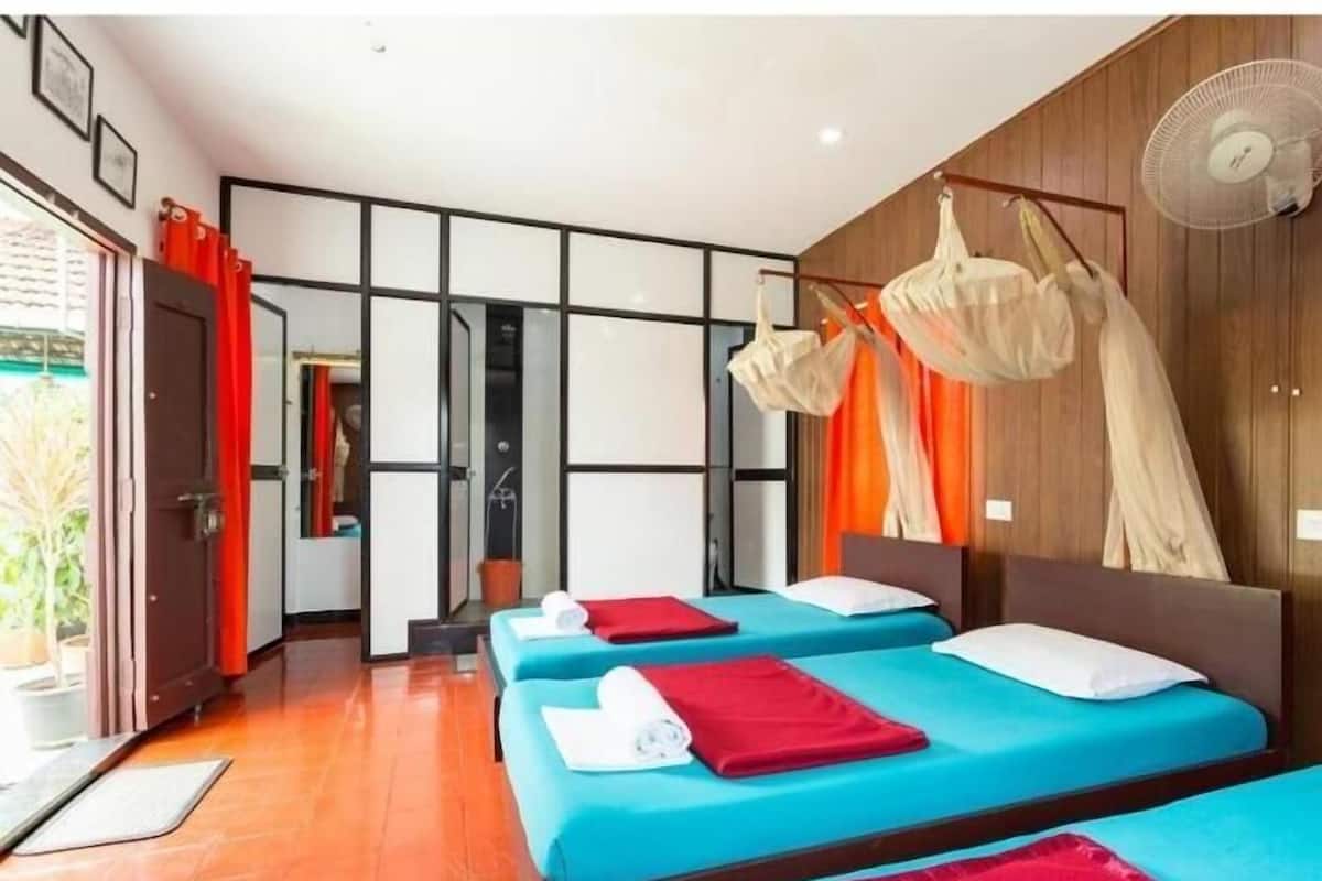 Quarto de hotel com duas camas, uma parede de destaque em madeira, ventoinha no teto e vista para o exterior.