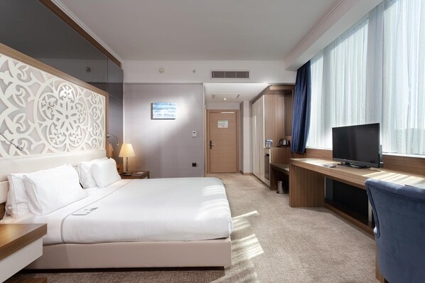 Quarto de hotel com uma cama grande, uma escrivaninha com televisão, um banheiro e um painel decorativo na parede.