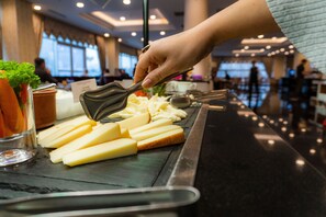 Uma pessoa cortando queijo em uma mesa de buffet em um hotel.