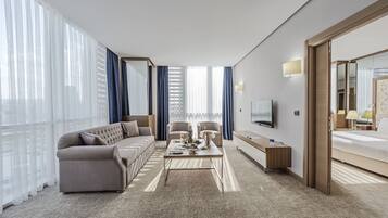 Quarto de hotel moderno com sofá, poltronas, mesa de centro, televisão e cama.