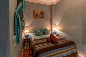 Quarto com cama, almofadas, manta, pintura e duas luminárias de cabeceira.