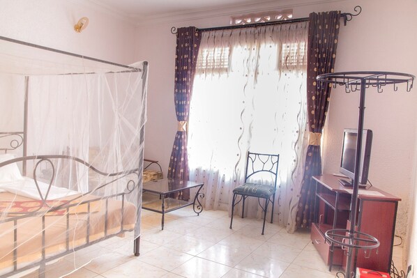 Quarto com cama de dossel, uma mesinha, uma cadeira, um rack para televisão e cortinas.