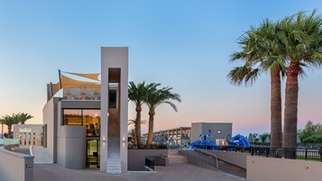 Um hotel moderno com estrutura em dois andares, entrada visível e área de piscina com guarda-sóis.