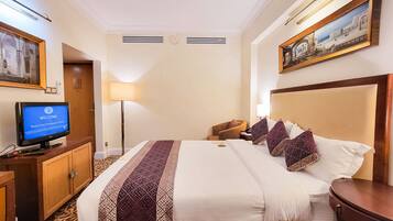 Quarto de hotel com uma cama, uma escrivaninha, uma televisão e um abajur.