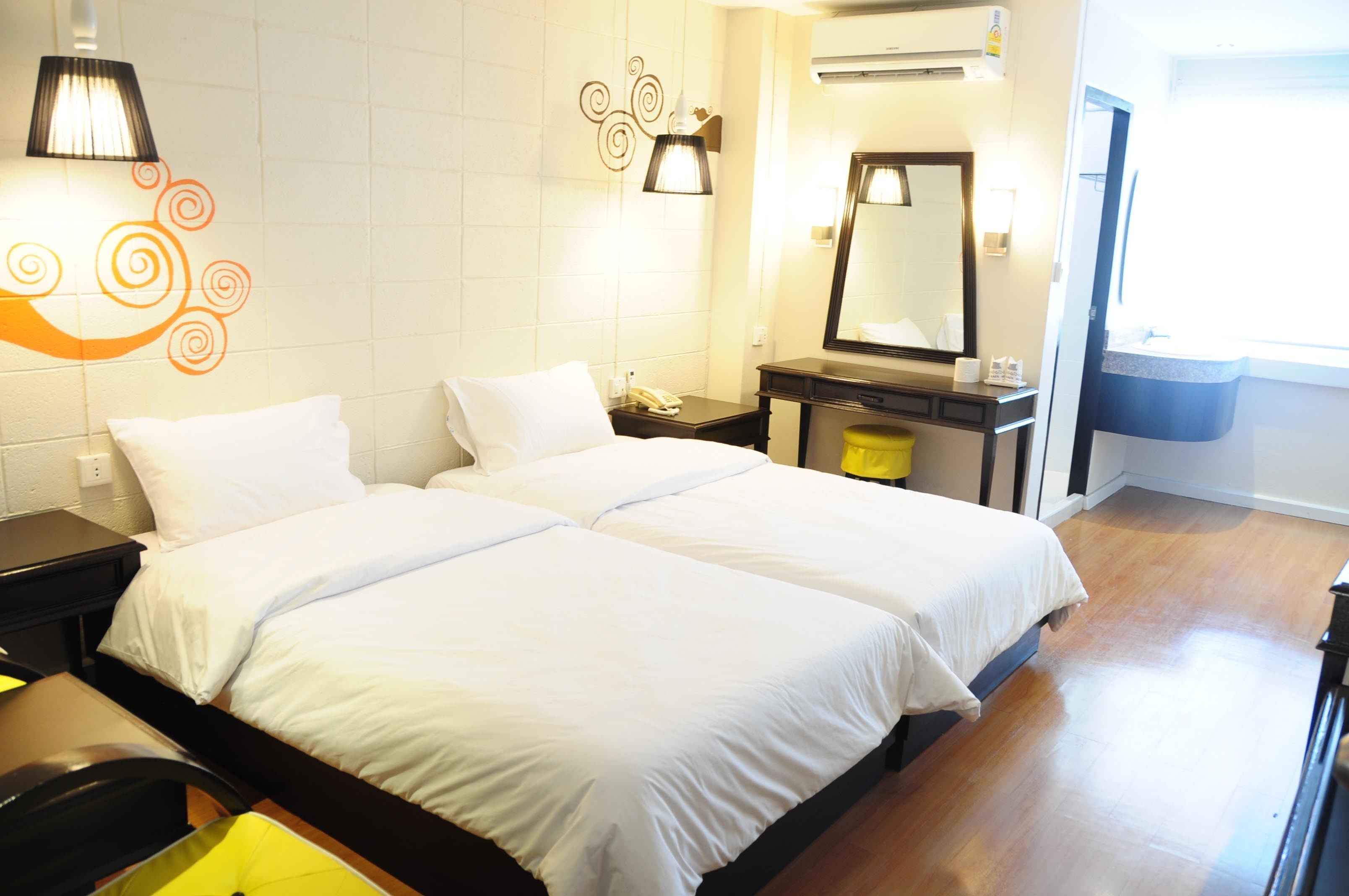 Quarto de hotel com duas camas, uma mesa de cabeceira com abajur, um espelho e uma janela.