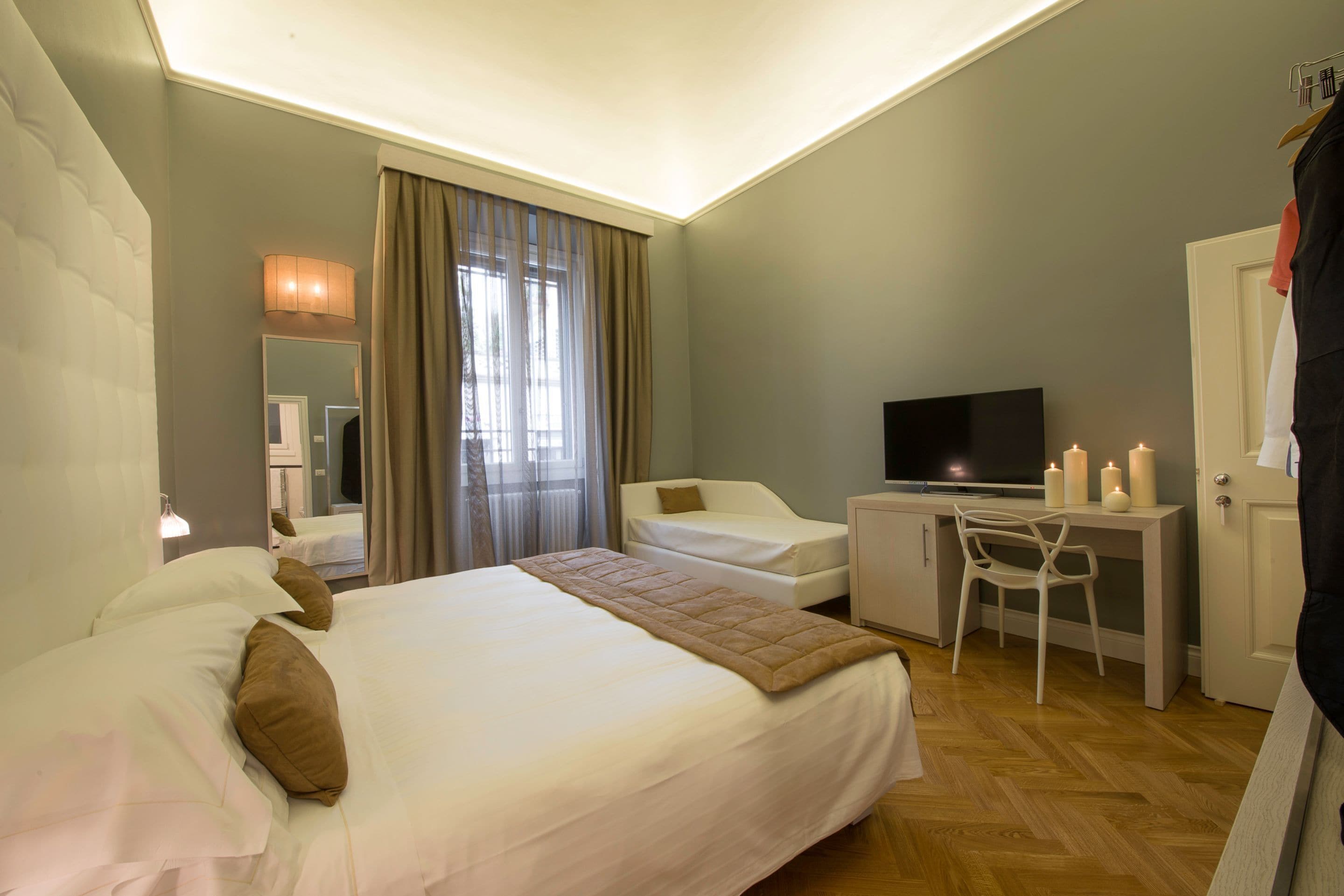 Quarto de hotel com cama, escrivaninha, televisão e espelho.