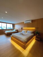 Quarto de hotel moderno com uma cama grande, uma cama menor e uma mesinha de cabeceira com uma planta.