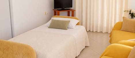 Quarto com cama, televisão, sofá e cortinas.
