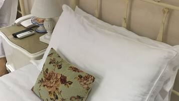 Cama bem arrumada com lençóis brancos e um travesseiro floral, mesa de cabeceira com abajur, telefone e controle remoto.