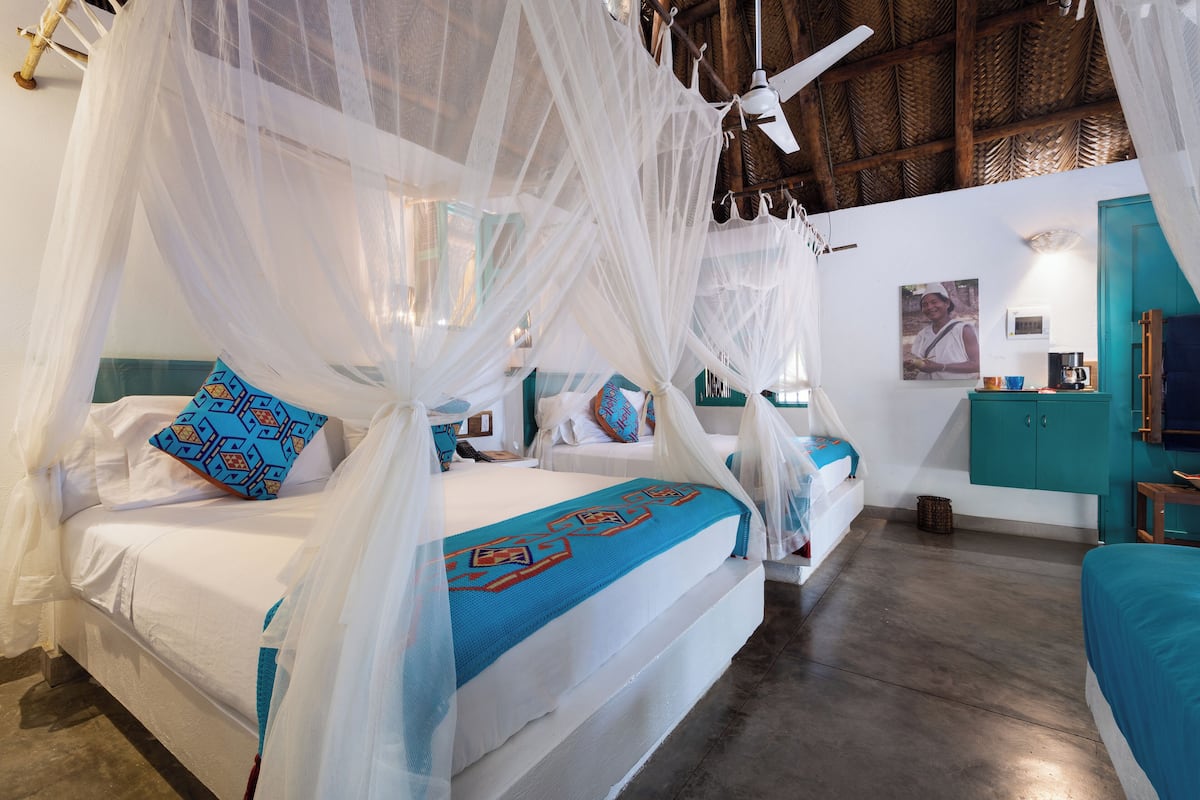 Quarto com cama sob uma rede mosquiteira, um ventilador de teto e um armário cor de verde-água.