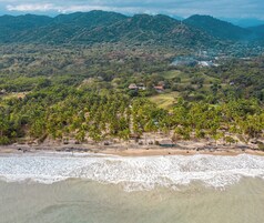 Paisagem costeira com praia, palmeiras e um horizonte montanhoso.