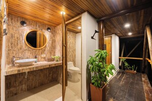 Uma casa de banho com toucador de madeira, espelho redondo, sanita e planta em vaso.