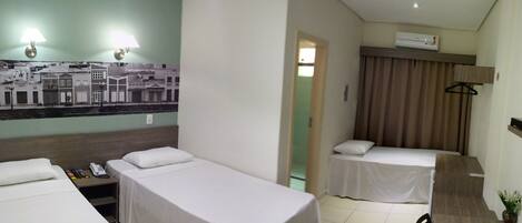 Quarto de hotel com duas camas de solteiro, uma mesinha com telefone, televisão na parede e um quadro com vista urbana.