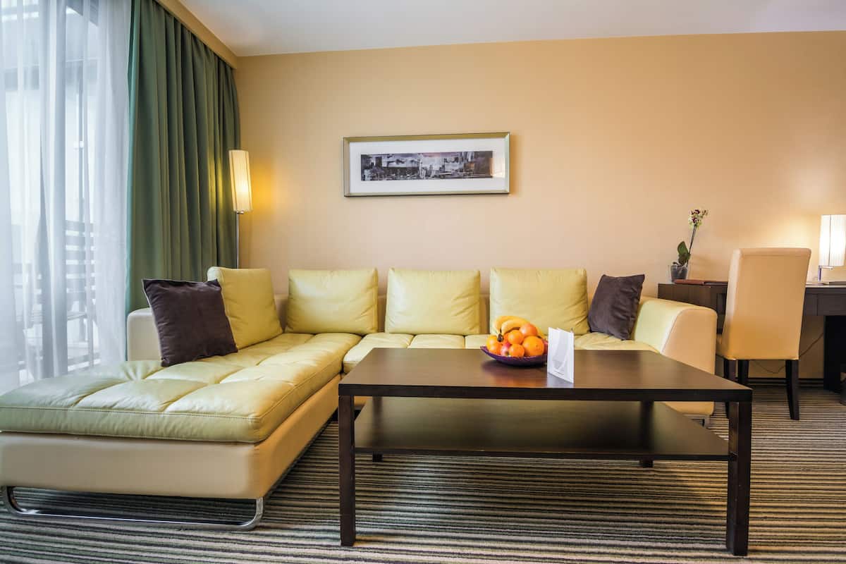 Quarto de hotel moderno com sofá modular, mesinha de centro com frutas, escrivaninha e quadro na parede.