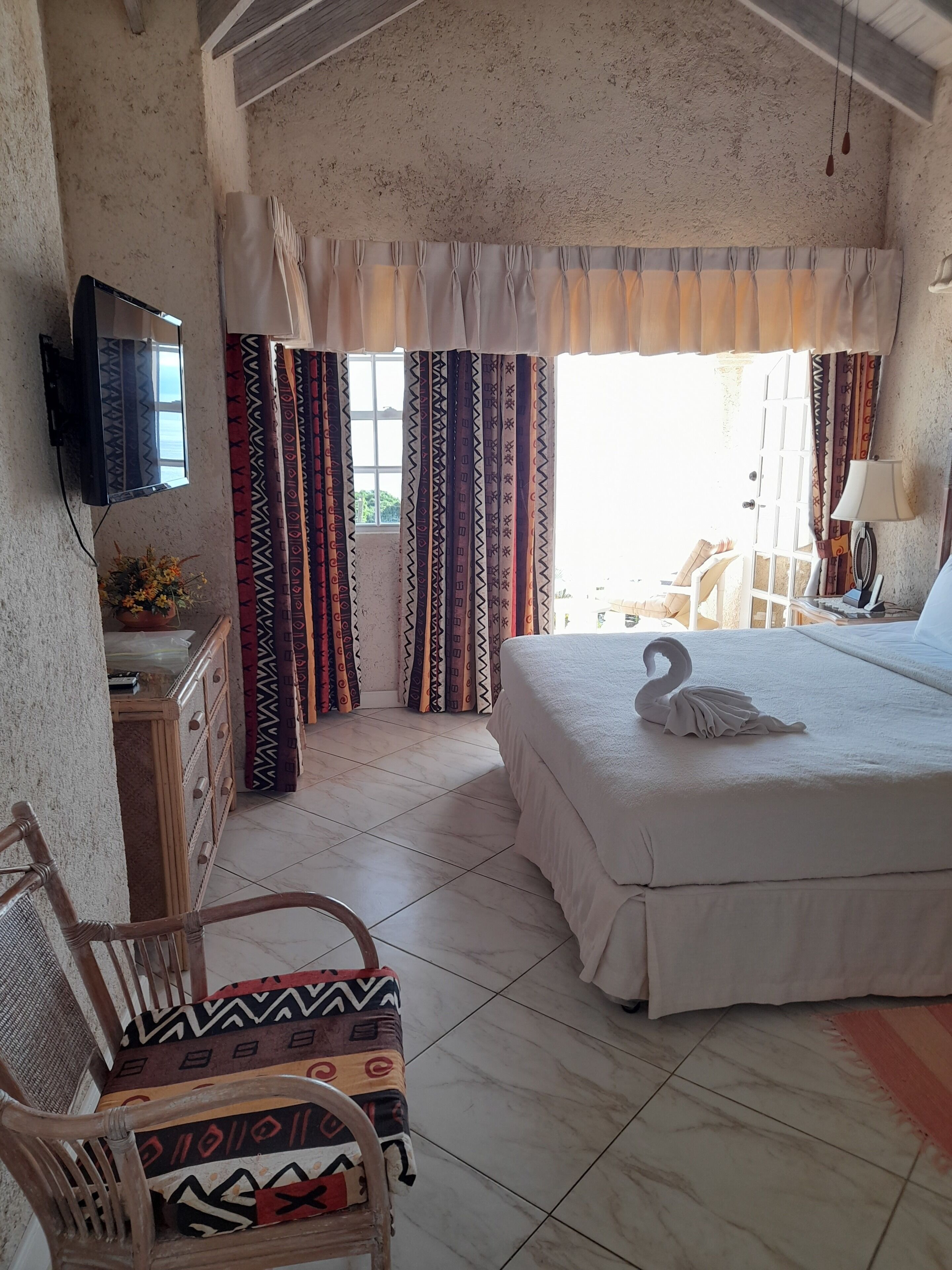 Um quarto com uma cama, televisão, cômoda, cadeira e cortinas.
