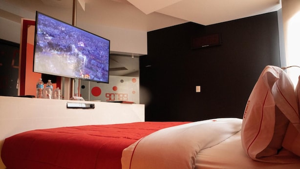 Quarto de hotel com uma cama, uma televisão fixada na parede e esquema de cores vermelho e branco.