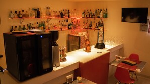 Uma área de bar com prateleiras de garrafas de bebidas, uma máquina de café e uma televisão na parede.