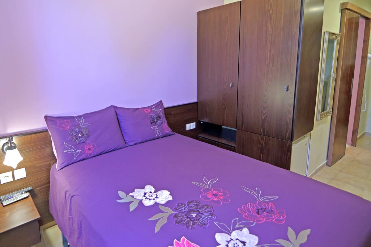 Quarto com uma cama grande, guarda-roupa de madeira e mesa de cabeceira com abajur.