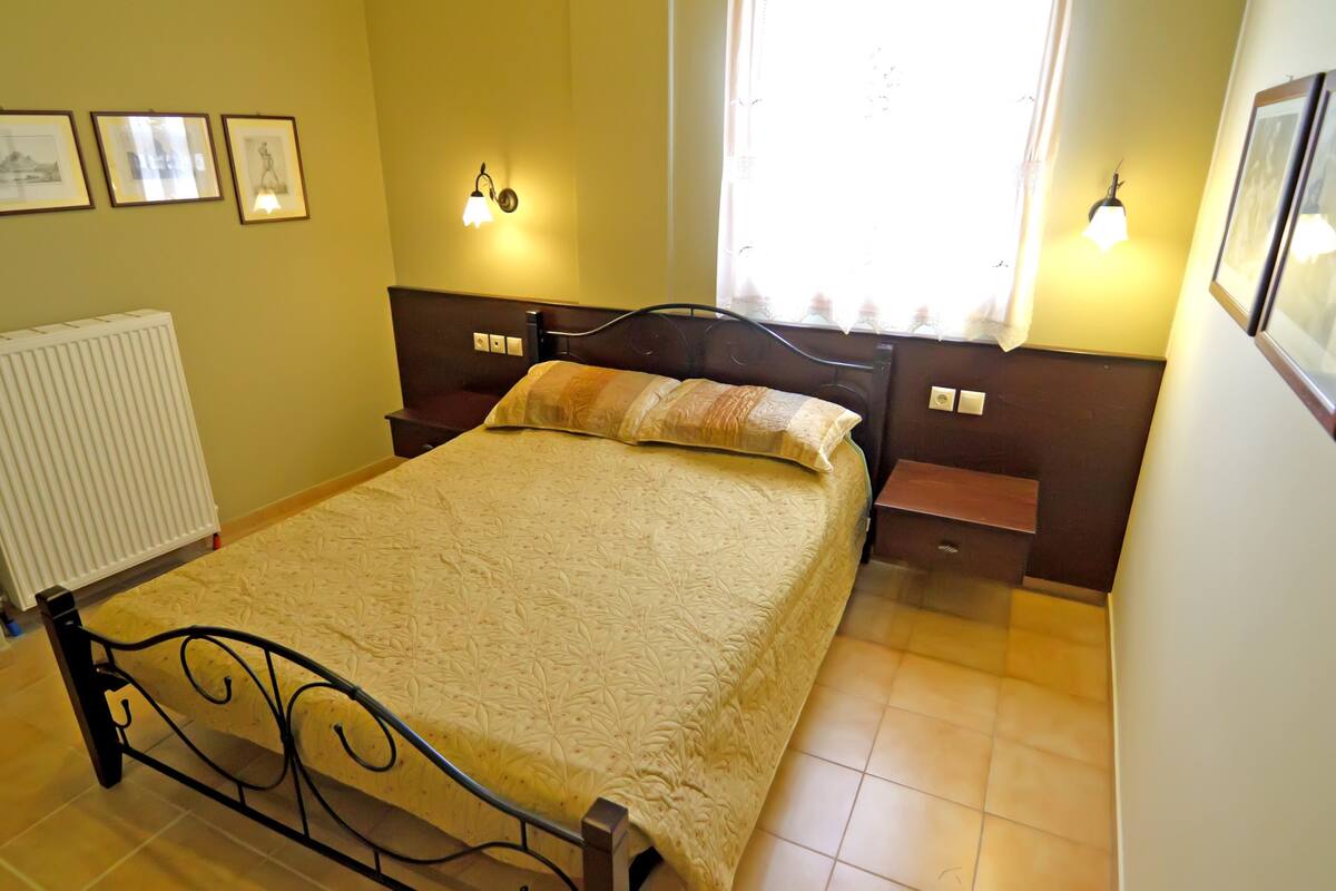 Quarto com cama, mesas de cabeceira, radiador e luzes fixadas na parede.