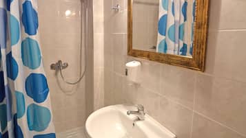Casa de banho com lavatório branco, chuveiro com cortina azul e espelho com moldura dourada.